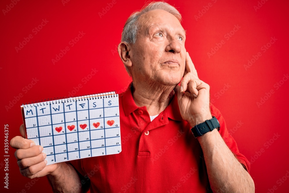 Senior grey haired man holding special date calendar over red ...