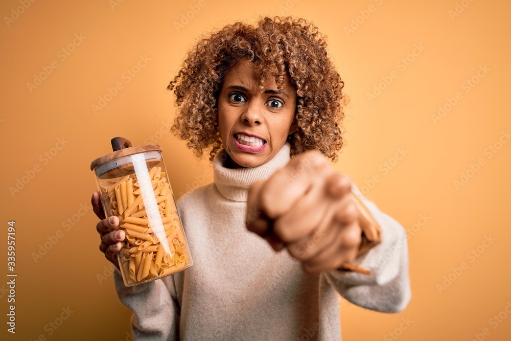 Young african american curly woman holding jar with Italian dry pasta ...