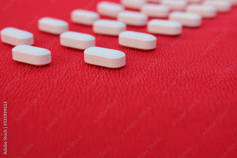 Medicine concept. White tablets are laid out in a line on a red ...