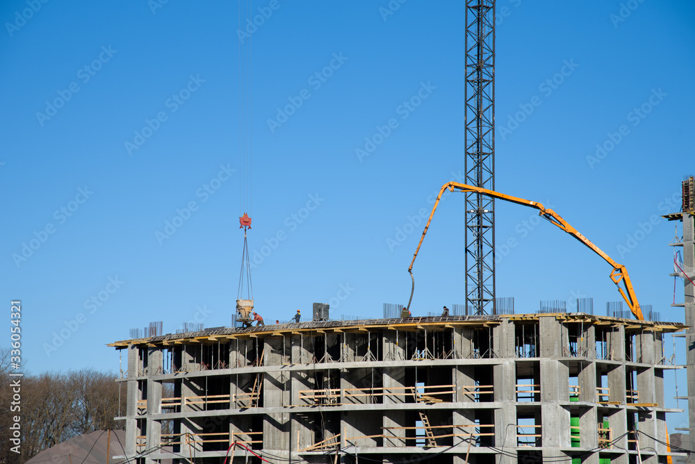 Tower crane lifting a concrete bucket at construction site. Workers ...