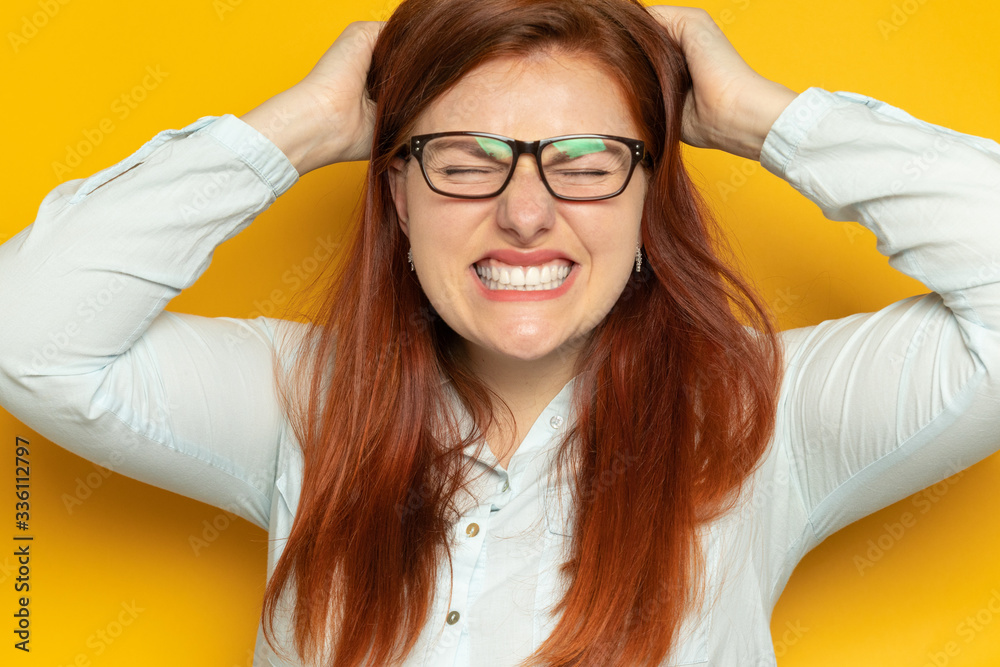 Crazy angry young girl in glasses holds herself by the head on a yellow ...
