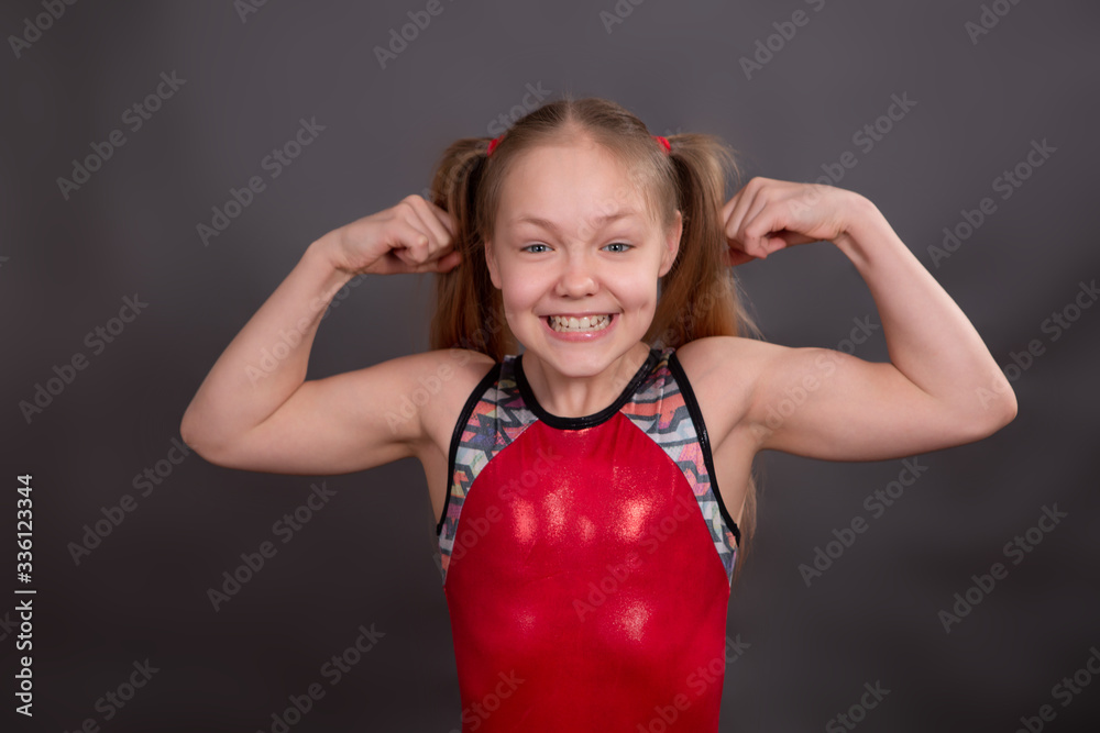 A girl athlete in a red sports swimsuit smiles and strains the muscles ...