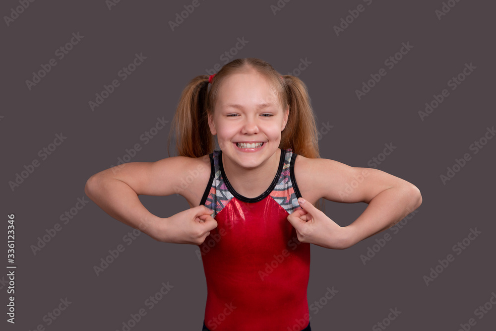 A girl athlete in a red sports swimsuit smiles and strains the muscles ...