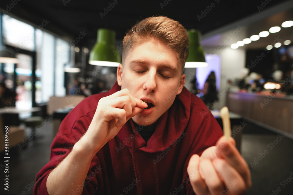 Close-up portrait of a hungry young man eating fries in front of a fast ...