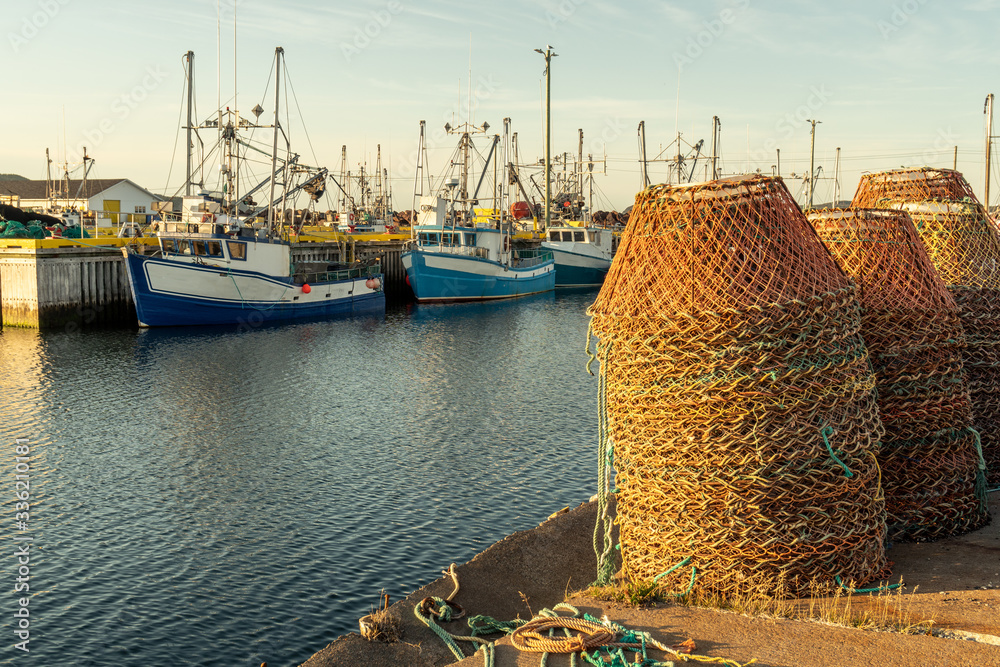 Piles of lobster pot traps on a deserted dock and fishing boats in a ...