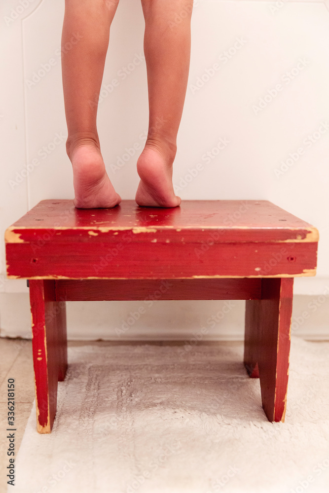 Closeup of the legs of a child standing on a step stool in the bathroom ...