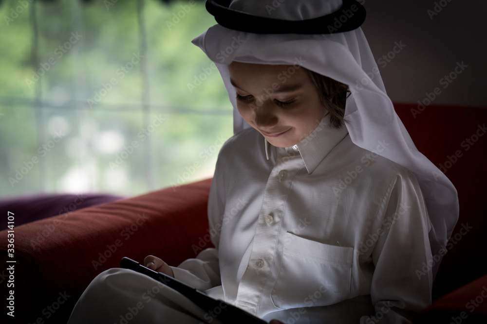 Cute Arabian kid sitting on sofa at home with tablet Stock Photo ...