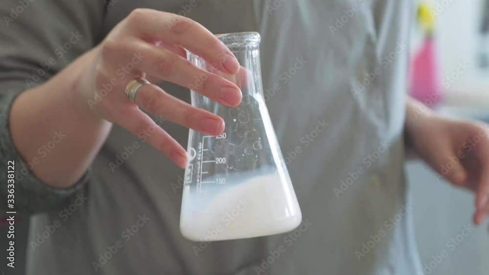 A woman shakes a glass flask to mix the components in it. There is a ...
