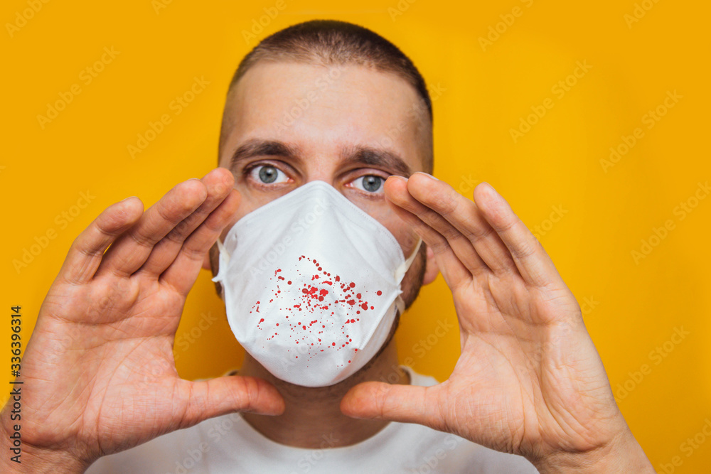 Young guy in a respirator on a yellow background. Coughs up blood ...