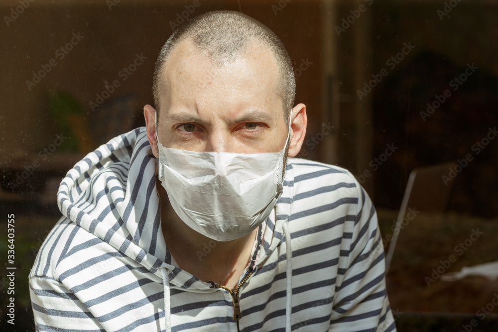 Sad bold man wearing face mask sitting by the bay window during his ...