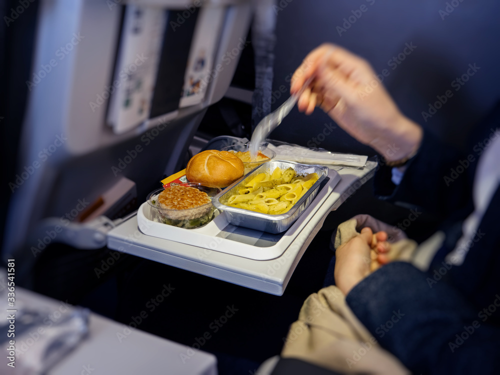 Side view of woman eating delicious meal in modern aircraft economy ...
