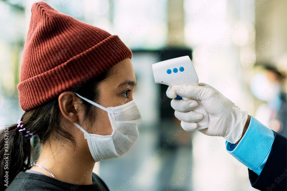 Woman in a medical mask getting her temperature measured by an ...