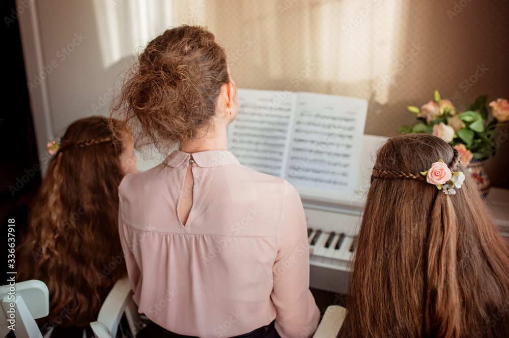 Home piano lesson. A woman and two girls practice sheet music on one ...