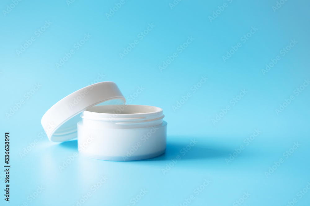 Open moisturizer cream in white plastic jar on blue background, front ...