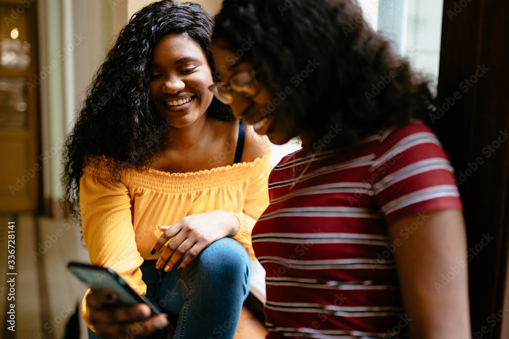 two girls laughing over something they're viewing on a mobile phone ...