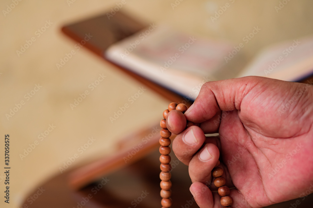 Hand holds tasbih or islamic prayer beads against quran on wooden book ...