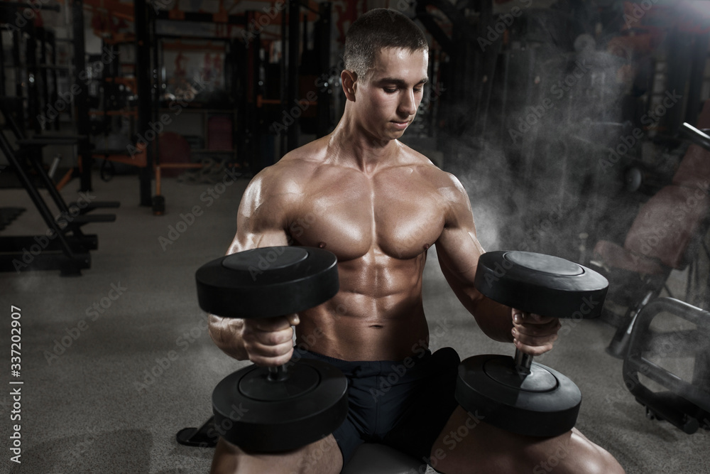 Athlete muscular bodybuilder in the gym training biceps with dumbbell ...