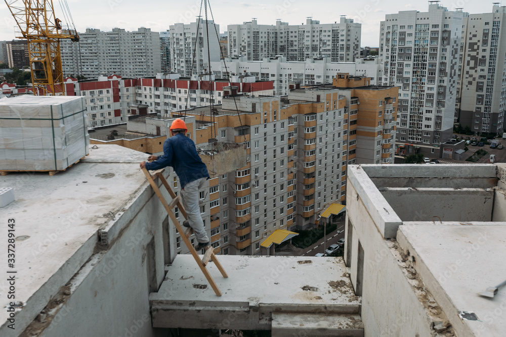 builder on the top floor of a building under construction in the middle ...