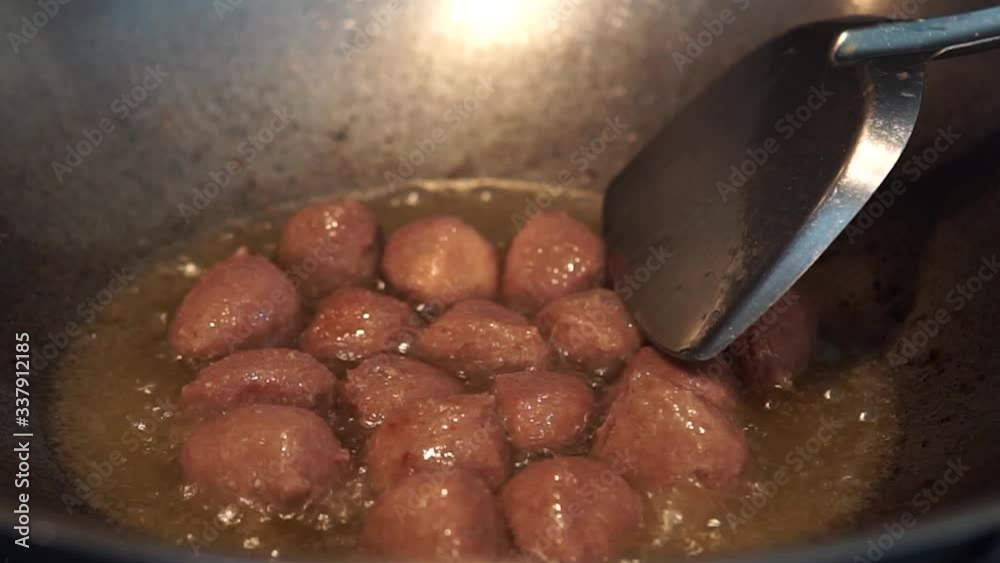 Frying a raw meatball in a hot boiling oil in a metal wok using a ...
