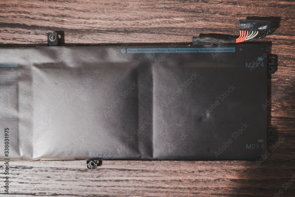 Swollen Lithium Polymer (Li-Po) laptop battery on a wooden table. Known ...