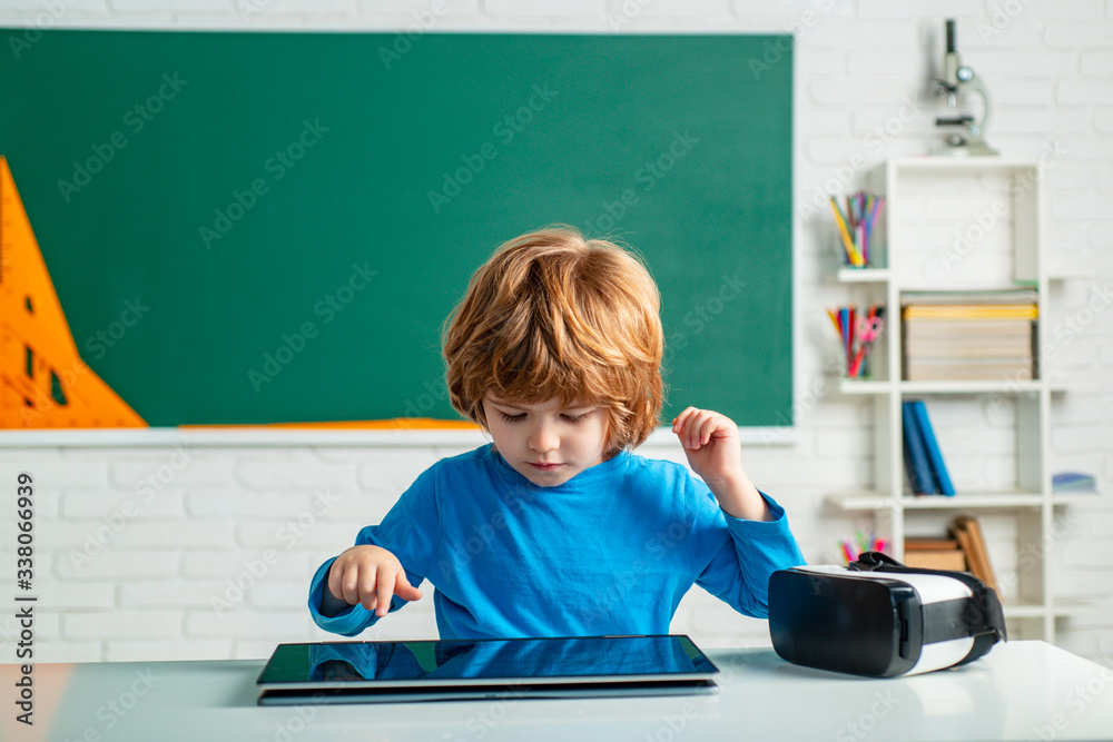 Schoolboy with digital tablet in school classroom. Pupil in class using ...