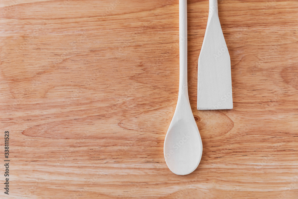 White wooden spoon and spatula lie next to each other on a light brown ...