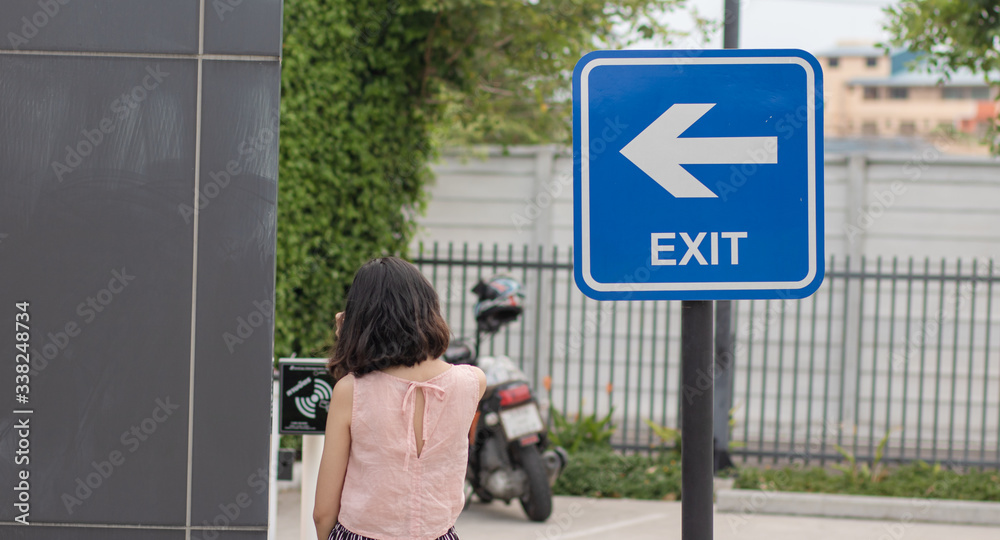 Woman standing with her back at the blue exit sign, metal exit sign ...