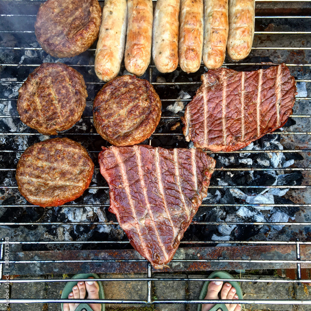 Barbequed steak, burgers and sausages cooking on a charcoal grill with ...