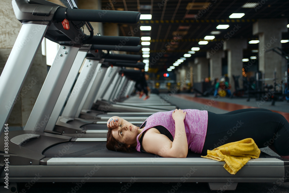 Tired overweight woman lying on treadmill in gym Stock Photo | Adobe Stock