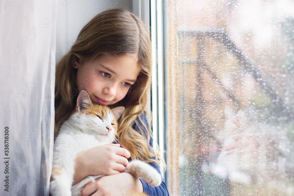 beautiful young girl sitting on the window with her cat in rainy day ...