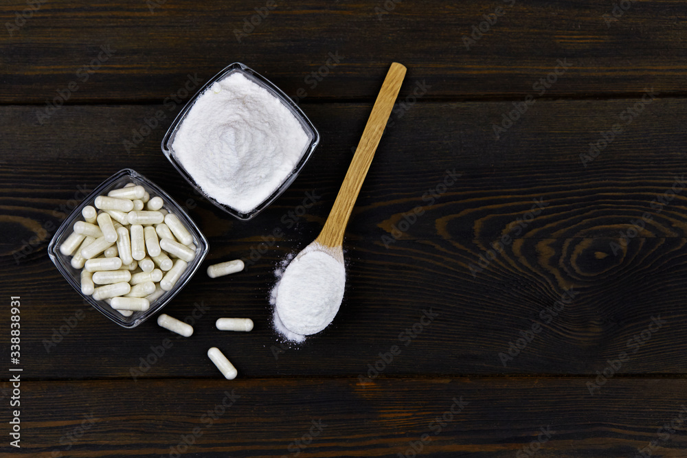 Collagen powder and collagen capsules in a spoon and jar on a dark ...
