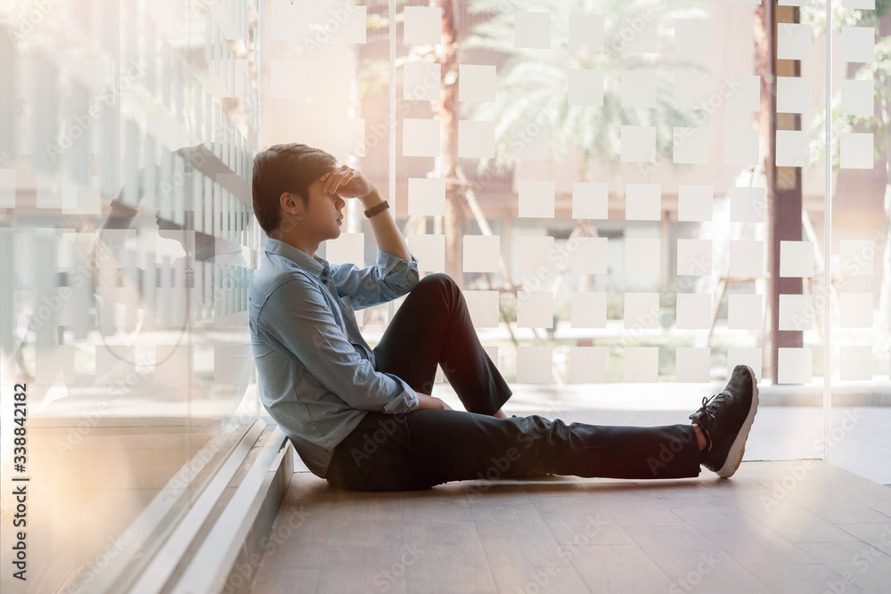 Sad man sitting on the floor by window at office walkway feeling ...