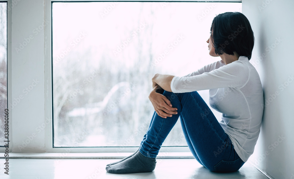 Self-isolation. Close-up photo of a sad woman who is hugging her knees ...