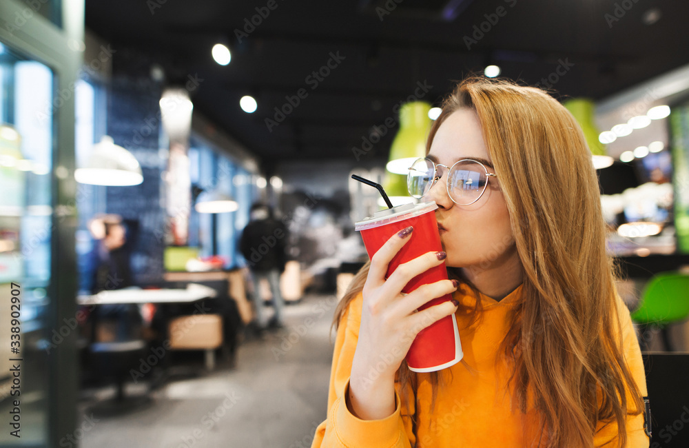 Cute girl in casual clothes in glasses sits at a fast food restaurant ...
