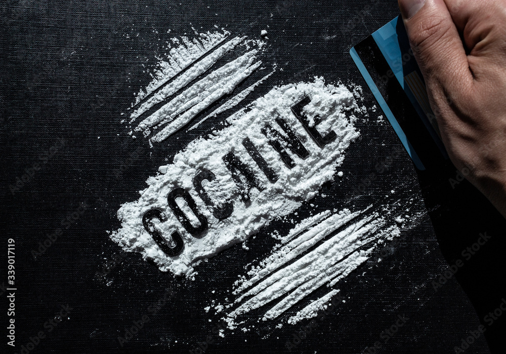 Closeup to a male hand hand holding a credit card making cocaine lines ...