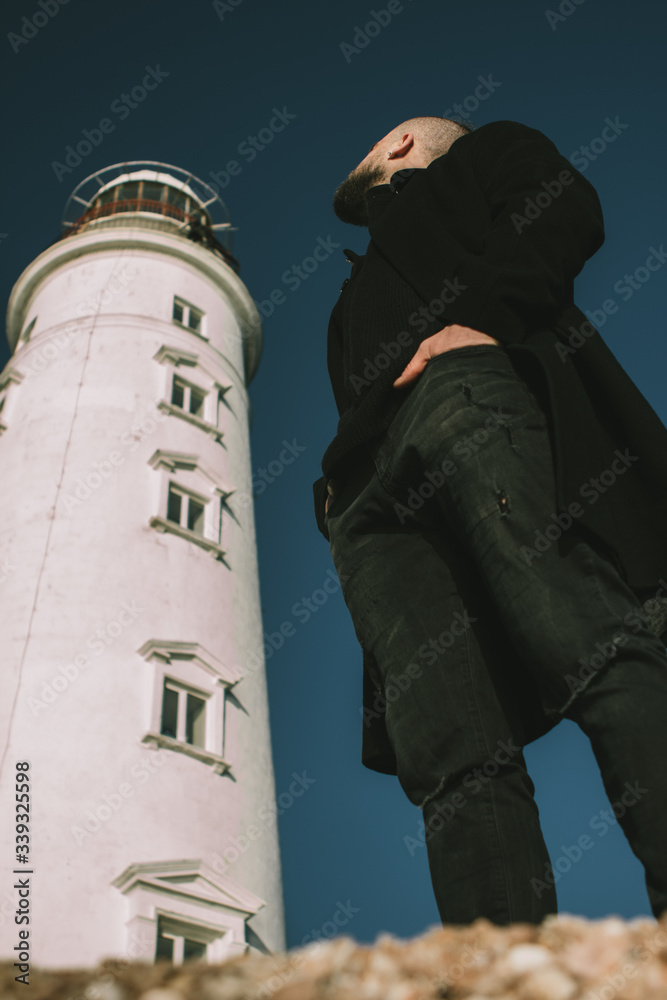 A guy in a black coat against a snow-white high lighthouse. Distortions ...