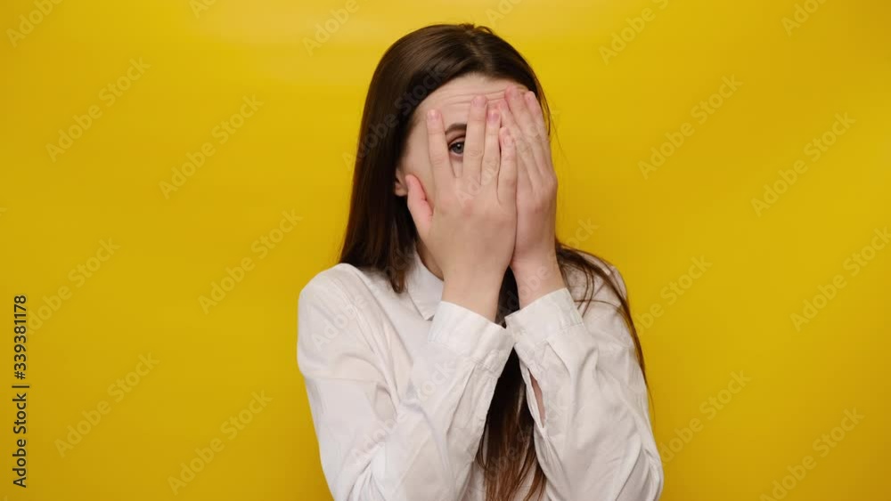 Scared young woman isolated on yellow studio background peep through ...