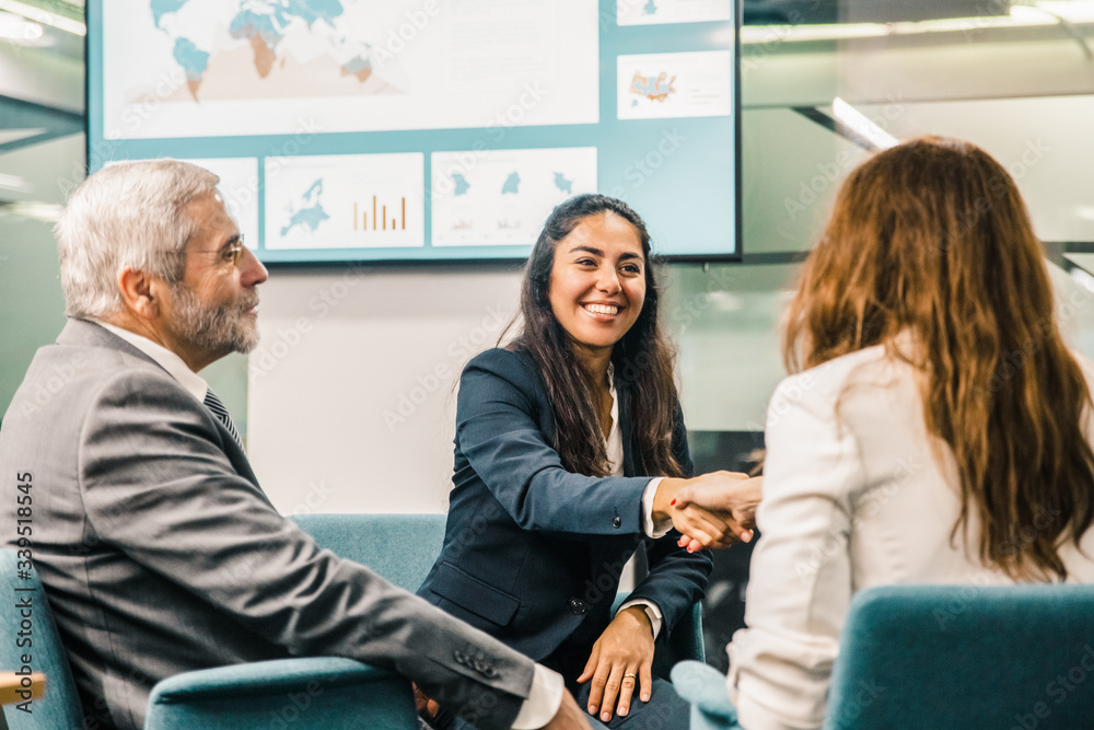 Confident female employees sitting on chairs and shaking hands ...