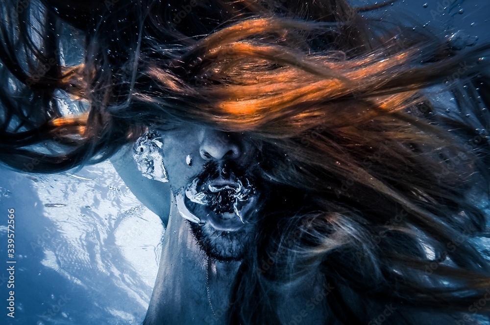 Artistic pic out of focus underwater with long hair man swimming with ...