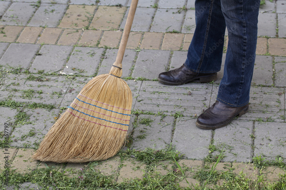 Women cleaning cut grass from pavement using classic broom made from ...