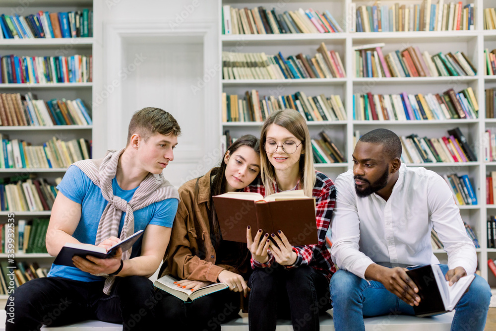 Happy four young university students studying with books in library ...