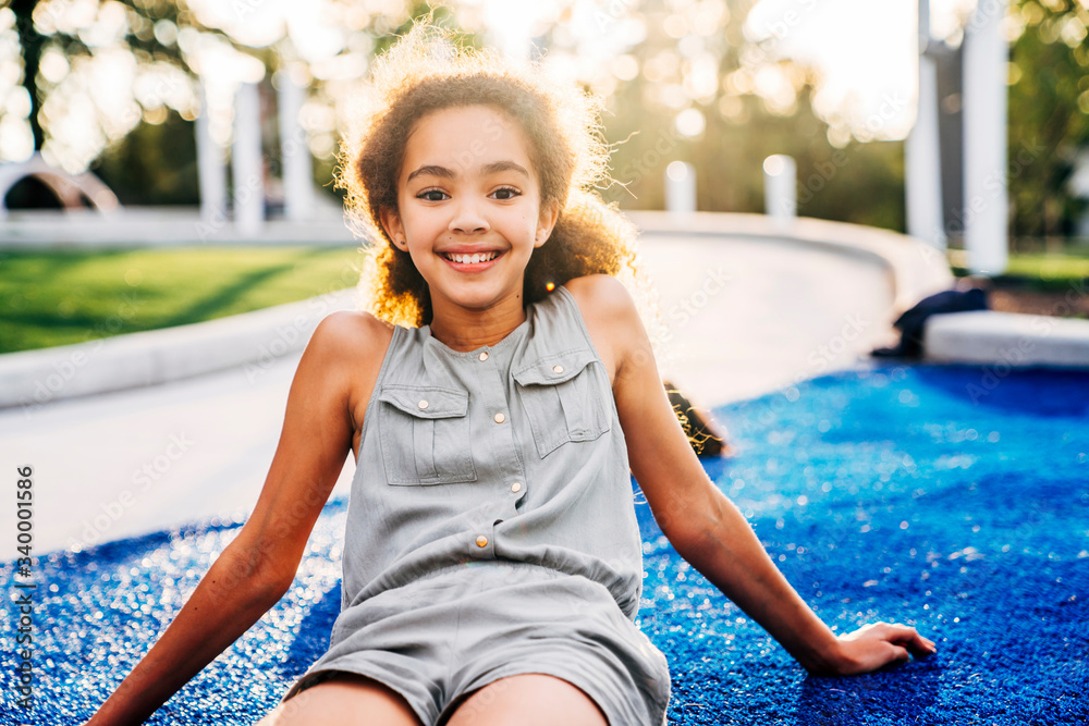 Portrait of smiling tween girl sitting in park at sunset Stock Photo ...