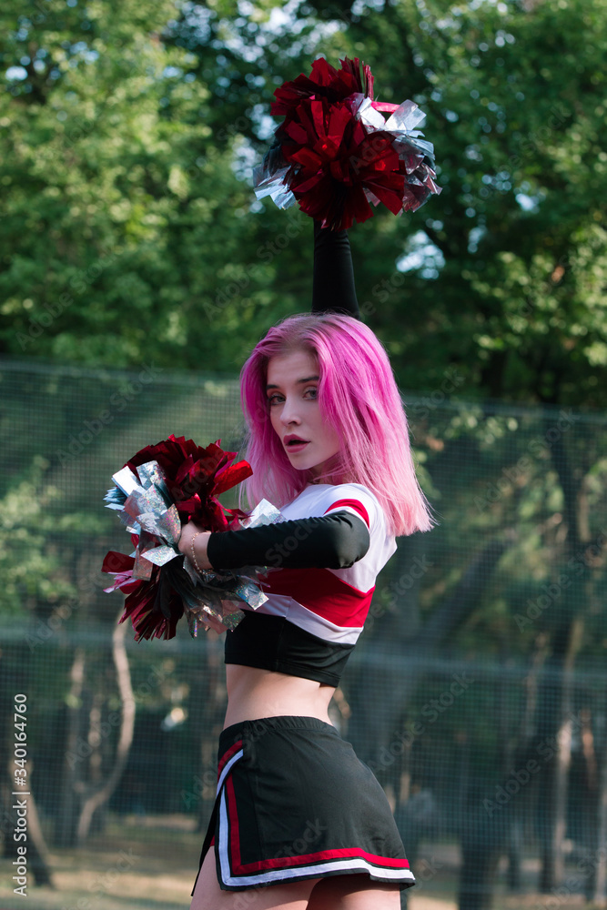 Slim fit girl cheerleader with pink hair dancing outdoors with red and ...