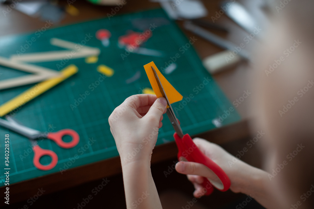 A five-year-old girl cuts out with a scissors yellow paper, craft with ...