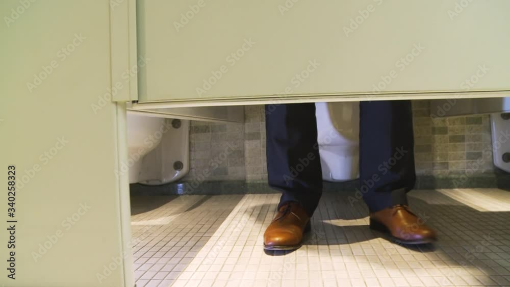 A man entering a washroom stall and sits on the toilet with his pants ...