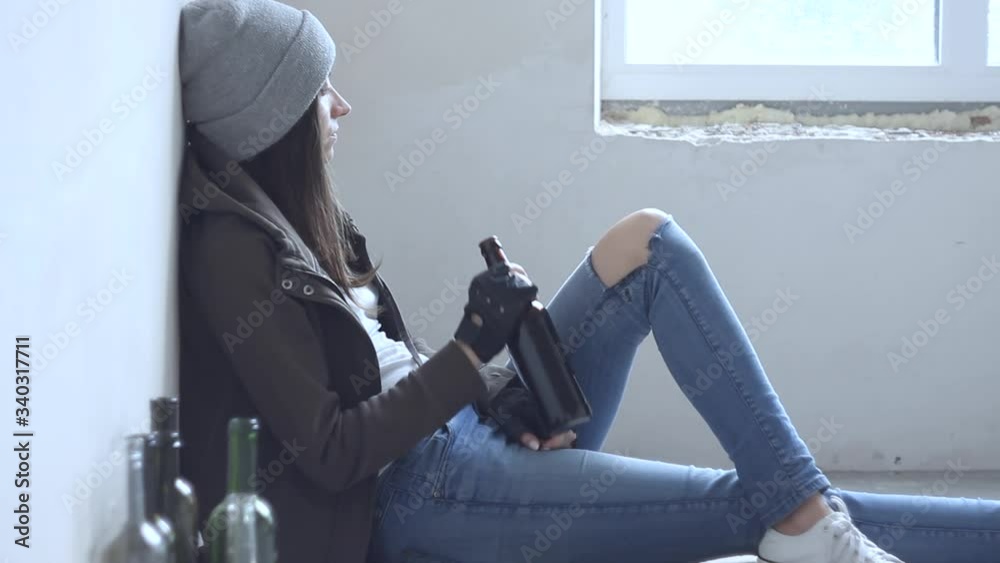 Homeless drunk woman is sitting on cardboard on floor in abandoned ...