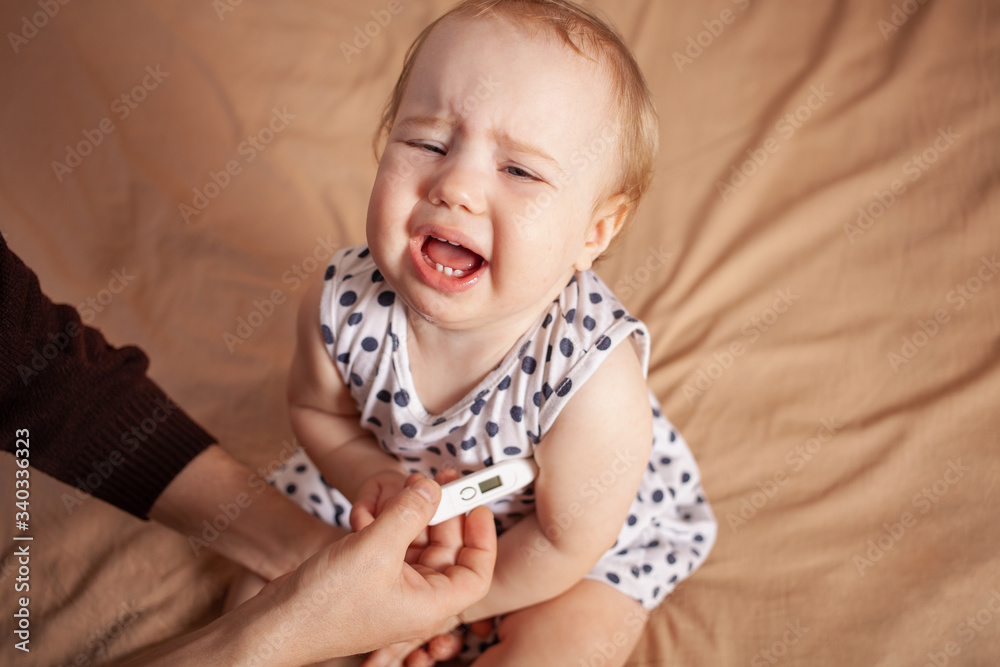 Sick child screams on the bed. Dad measures the temperature of his ...