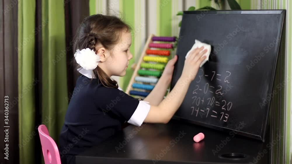 A schoolgirl wipes a blackboard with a wet rag, removing math examples ...