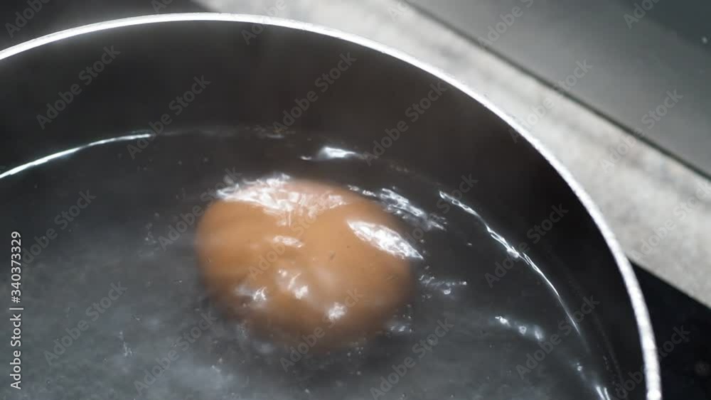 An egg in simmering hot water which is reaching boiling hot temperature ...