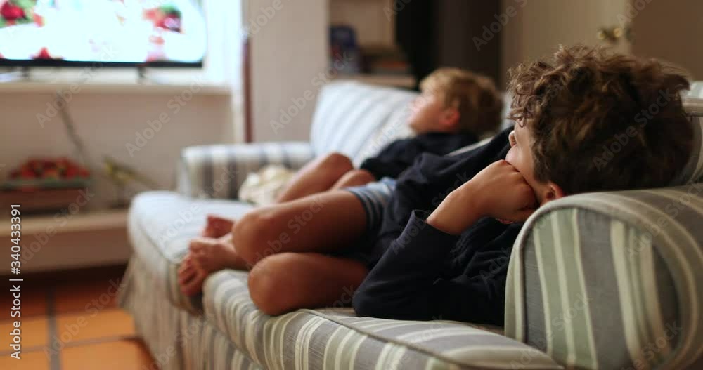 Children watching movie at night. Two brothers lying on couch staring ...